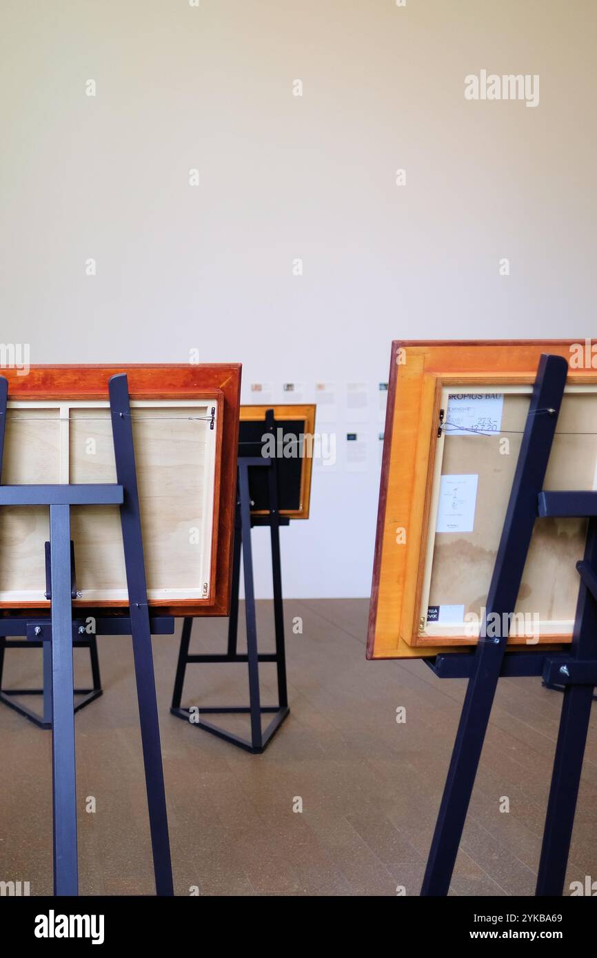 Wooden easels at a museum art exhibit seen from behind; rear view of ...