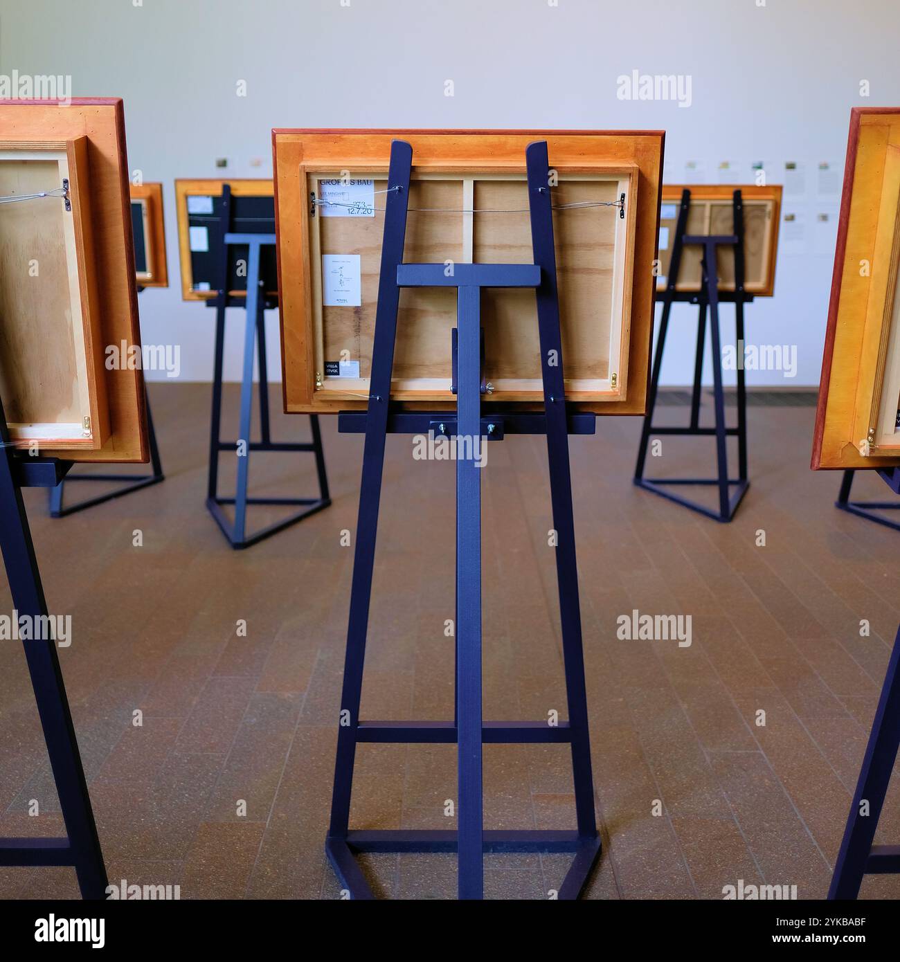 Wooden easels at a museum art exhibit seen from behind; rear view of ...