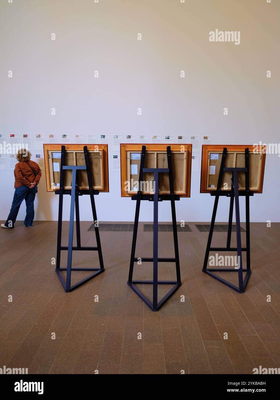 Museum patron viewing art with wooden easels at an art exhibit seen ...