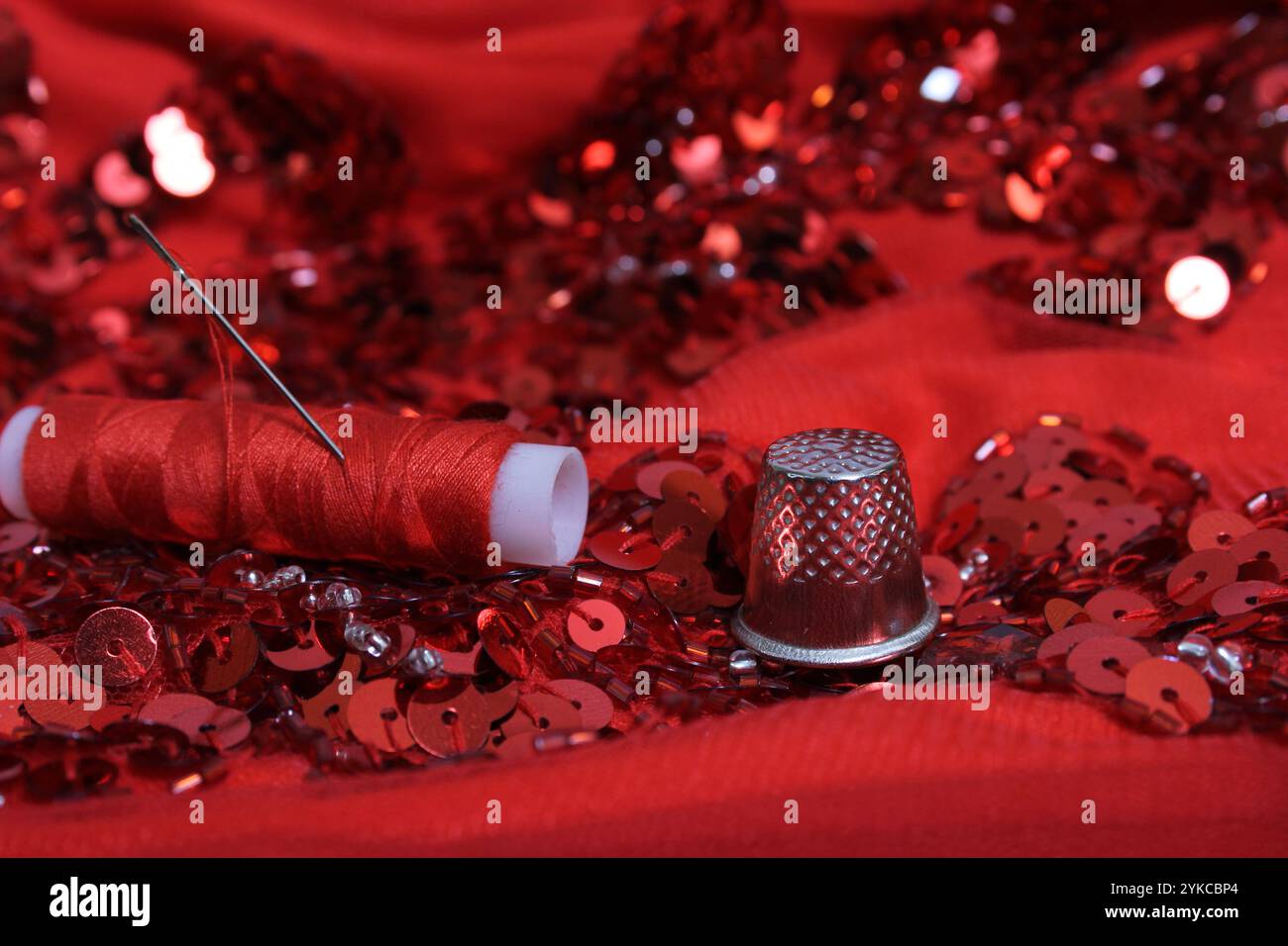 Red Beaded Fabric With Spool of Red Thread and Thimble Stock Photo - Alamy