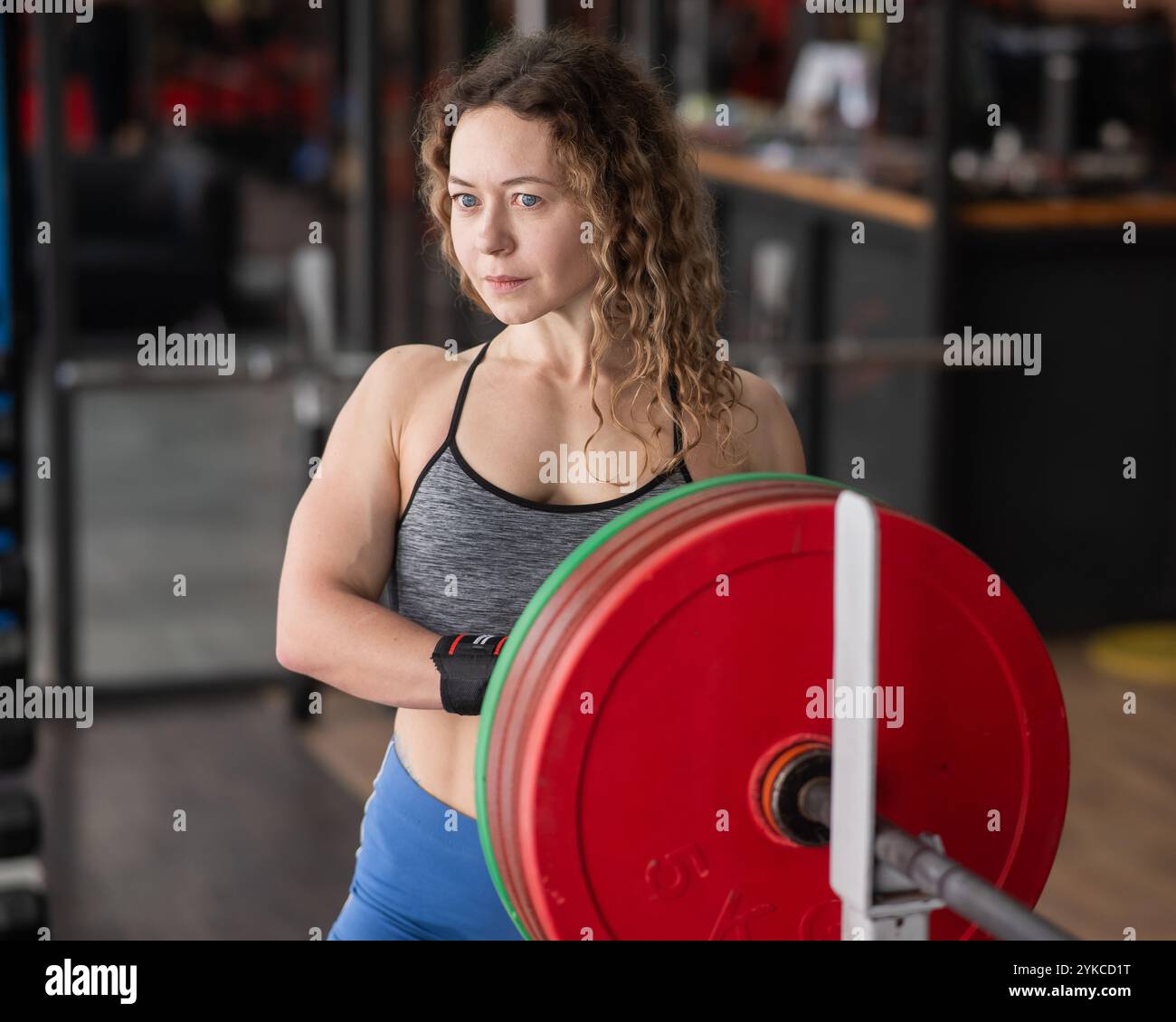 Caucasian forty year old woman putting a weight plate on a barbell in ...