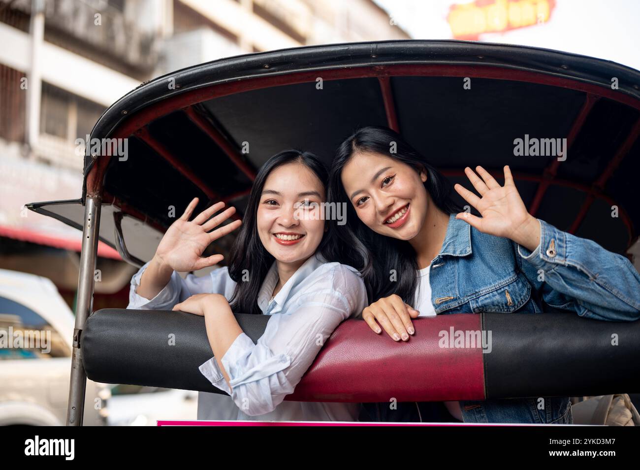 Two cheerful, charming young Asian girls enjoy a ride in a tuk-tuk in ...