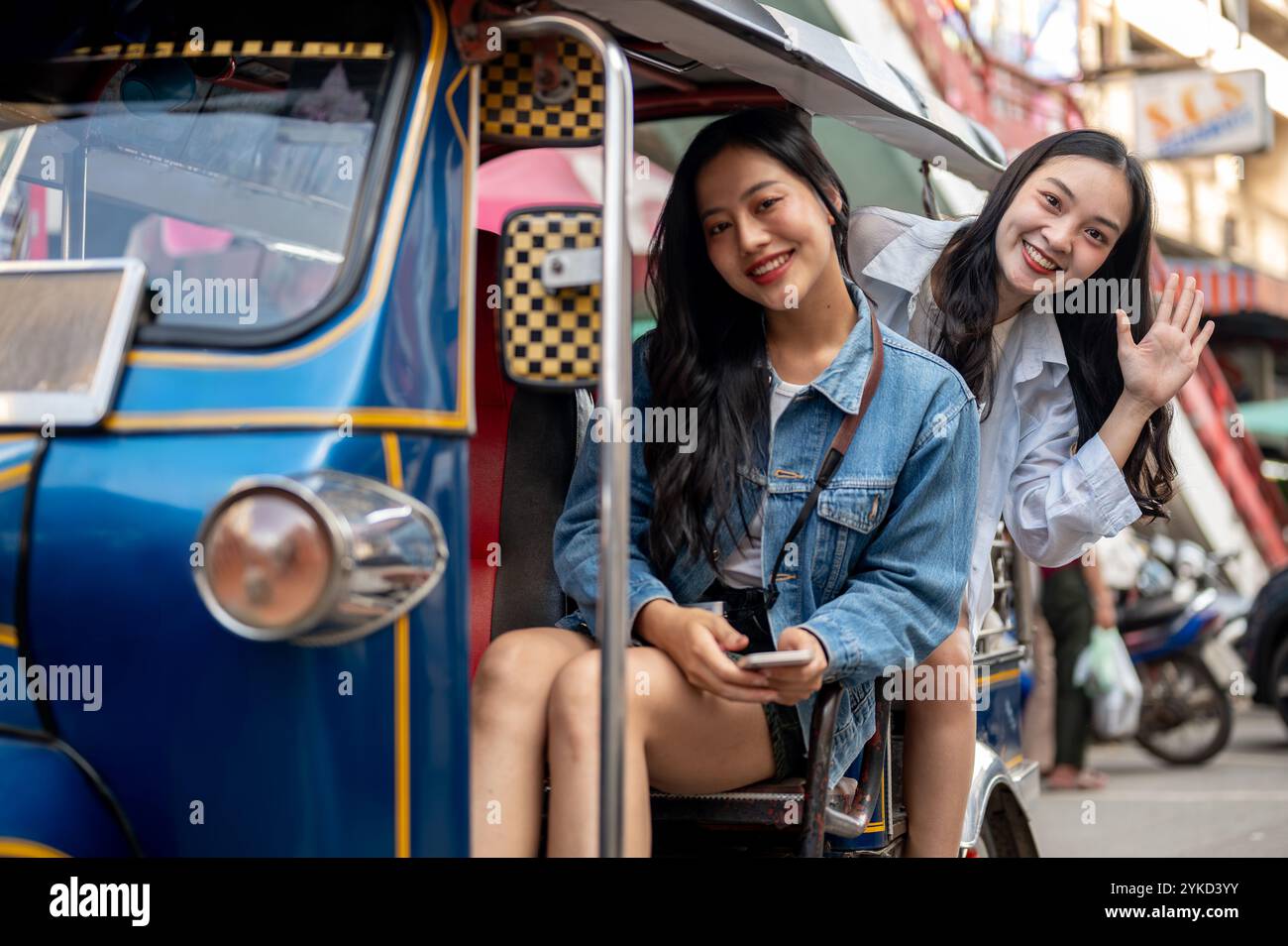 Two pretty and cheerful Asian women enjoy a tuk-tuk ride in Thailand ...