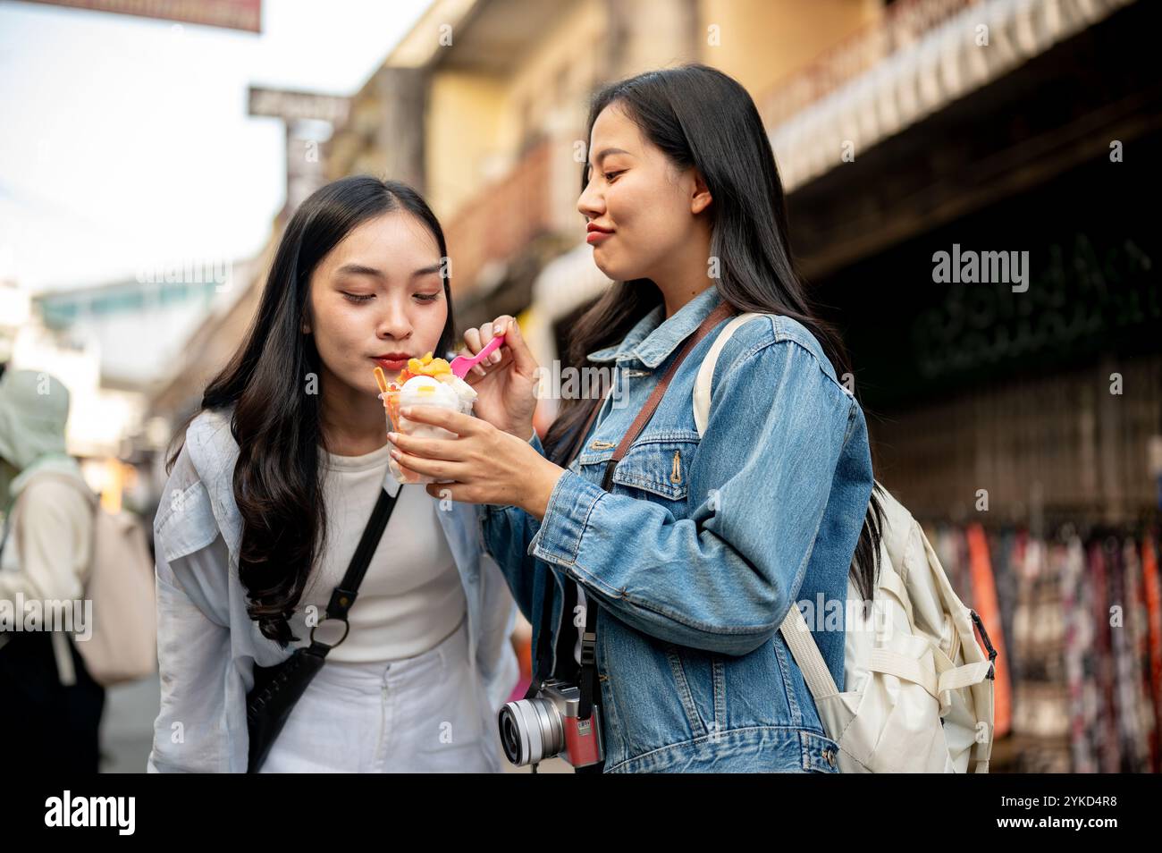 Two pretty, joyful young Asian female tourists enjoy street food at a ...