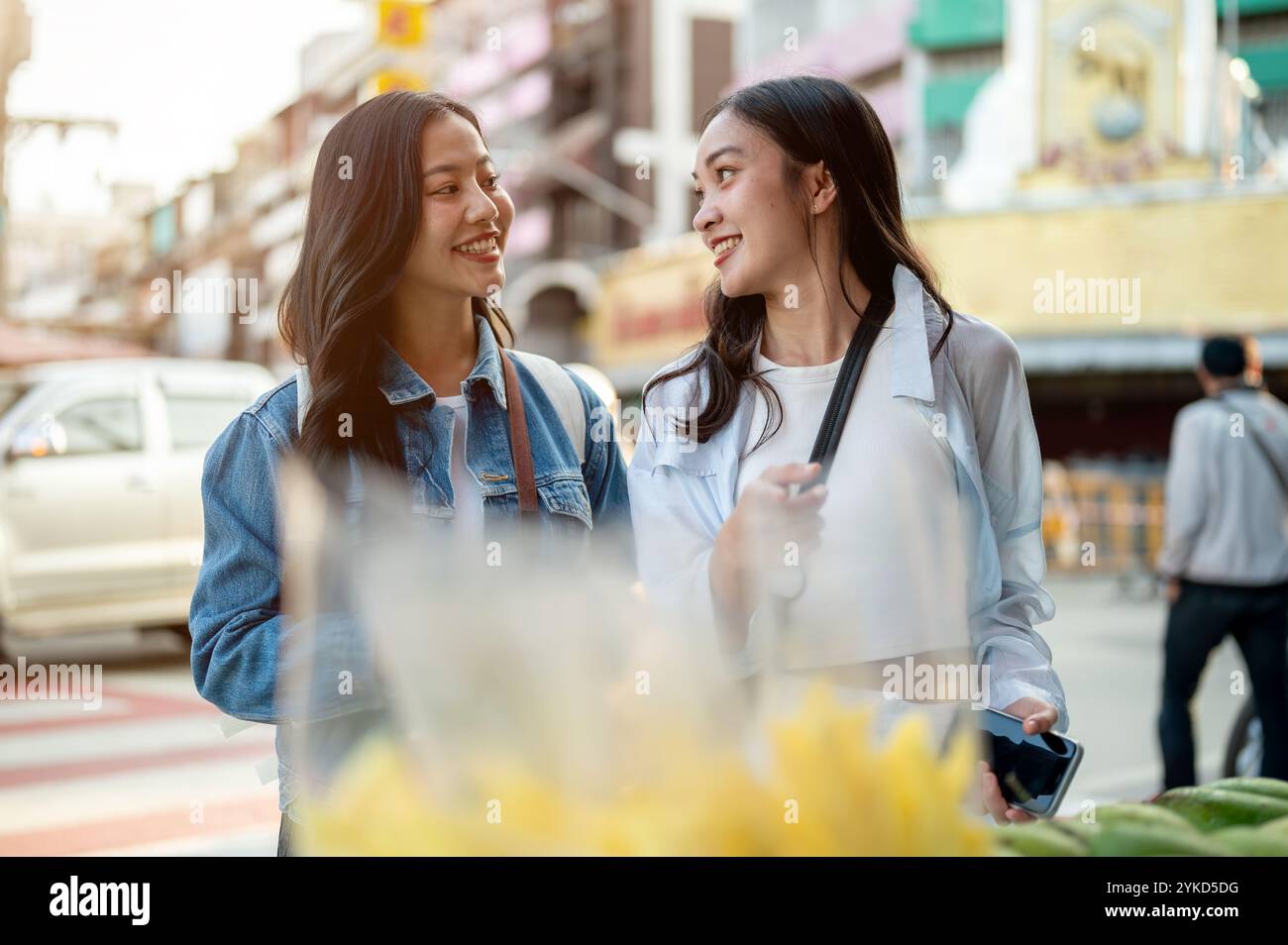 Two cheerful, cute Asian female tourists buy street food in Thailand ...
