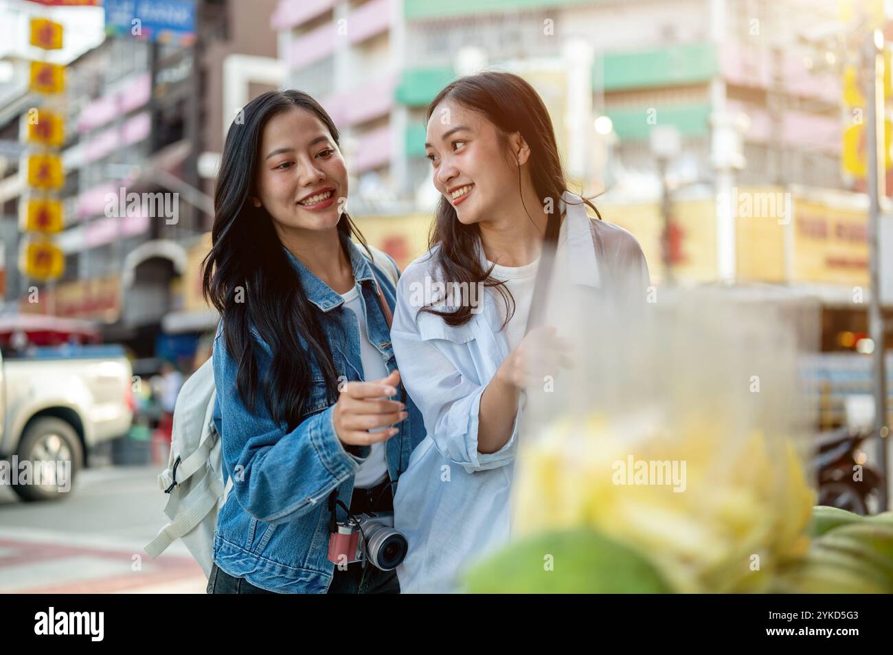 Two cheerful, cute Asian female tourists buy street food in Thailand ...