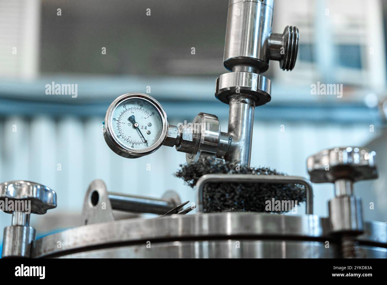 A pressure gauge on a stainless steel tank in an industrial setting ...