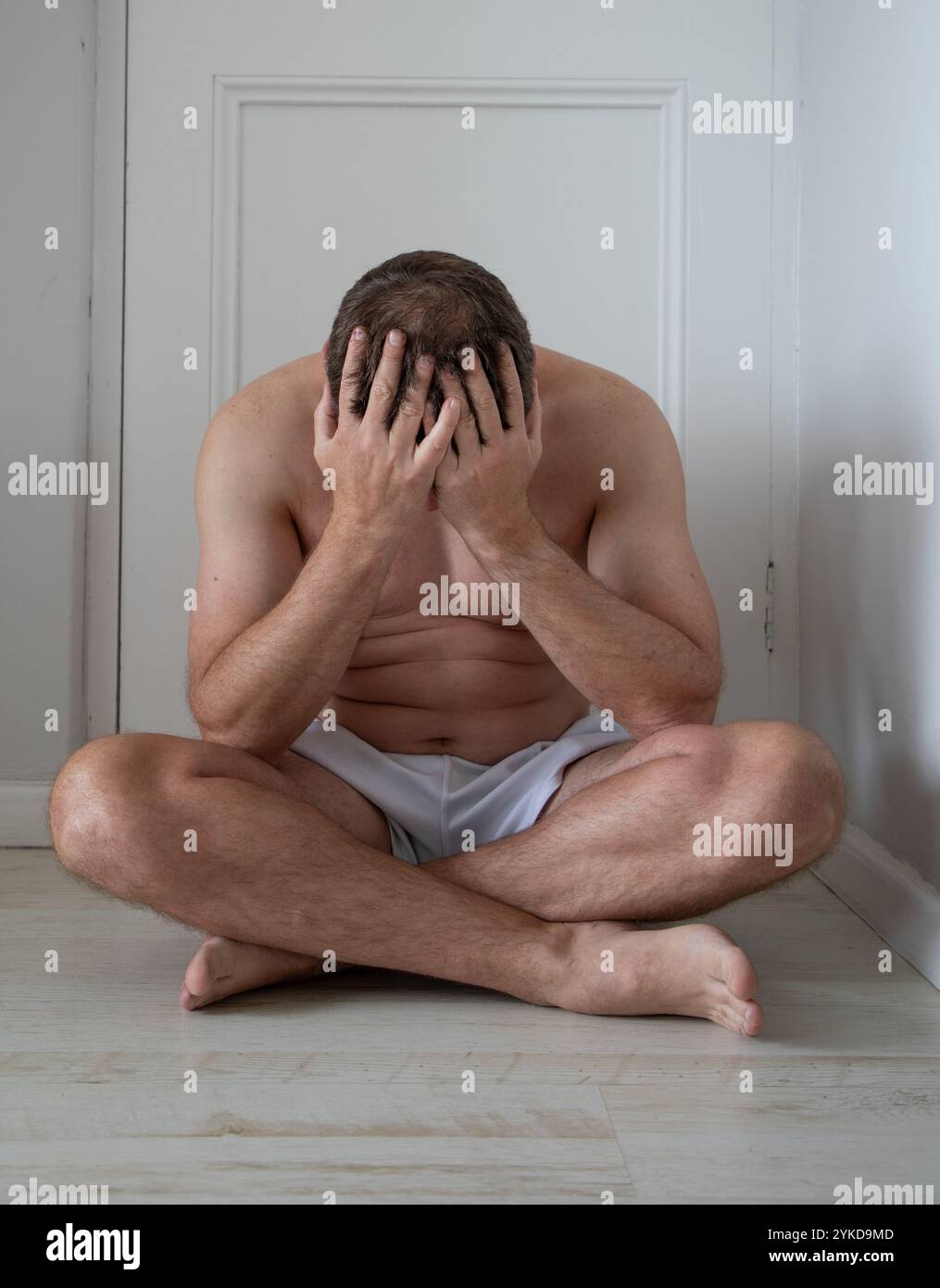 Caucasian man sitting on the floor, dressed in white shorts, with his legs crossed and hands ...