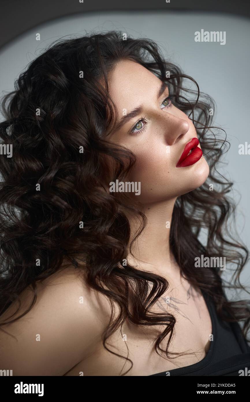 young woman with luscious curly hair and striking red lips poses ...