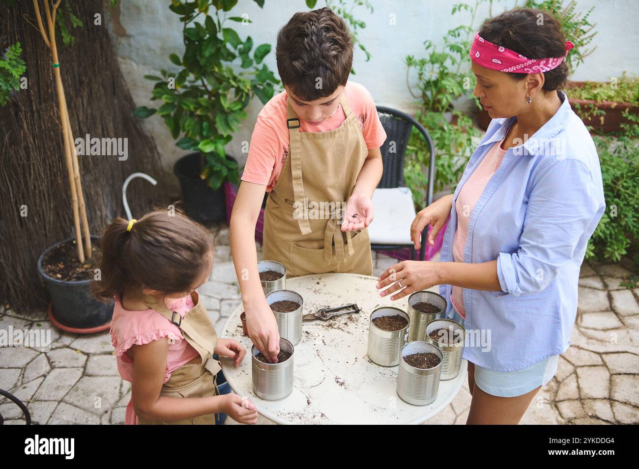 A family gardening session with children planting seeds in tin cans ...