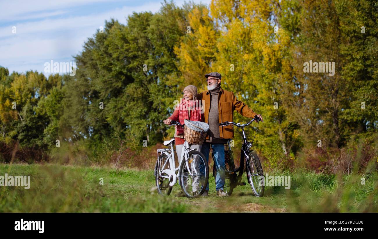 Lovely elderly couple on a walk in the forest, pushing their bikes side ...