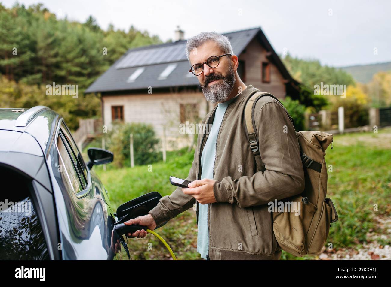 Man charging electric car in front of his house, plugging the charger ...