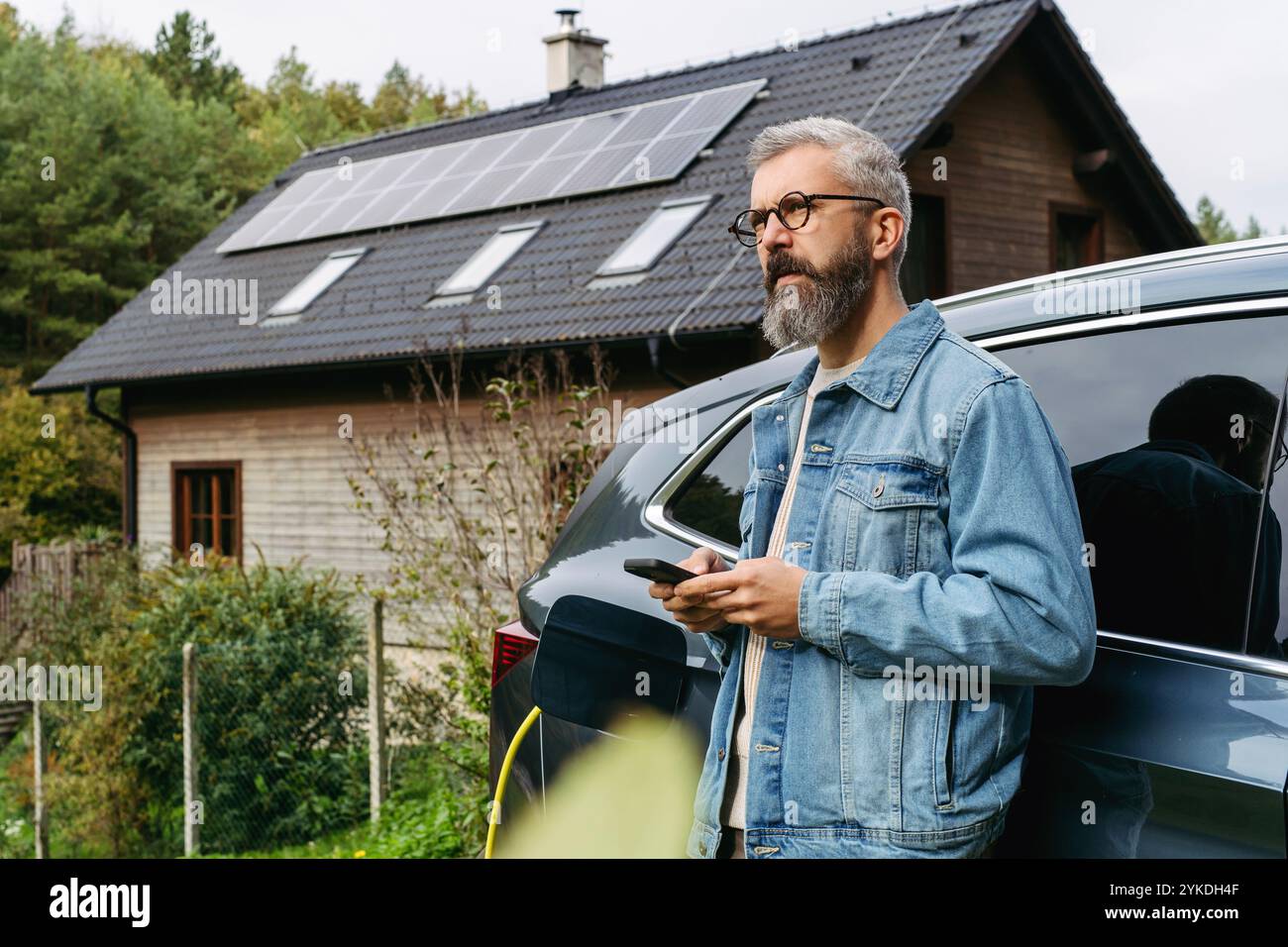 Man charging electric car in front of his house, plugging the charger ...