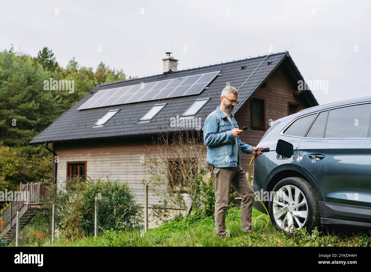 Man charging electric car in front of his house, plugging the charger ...