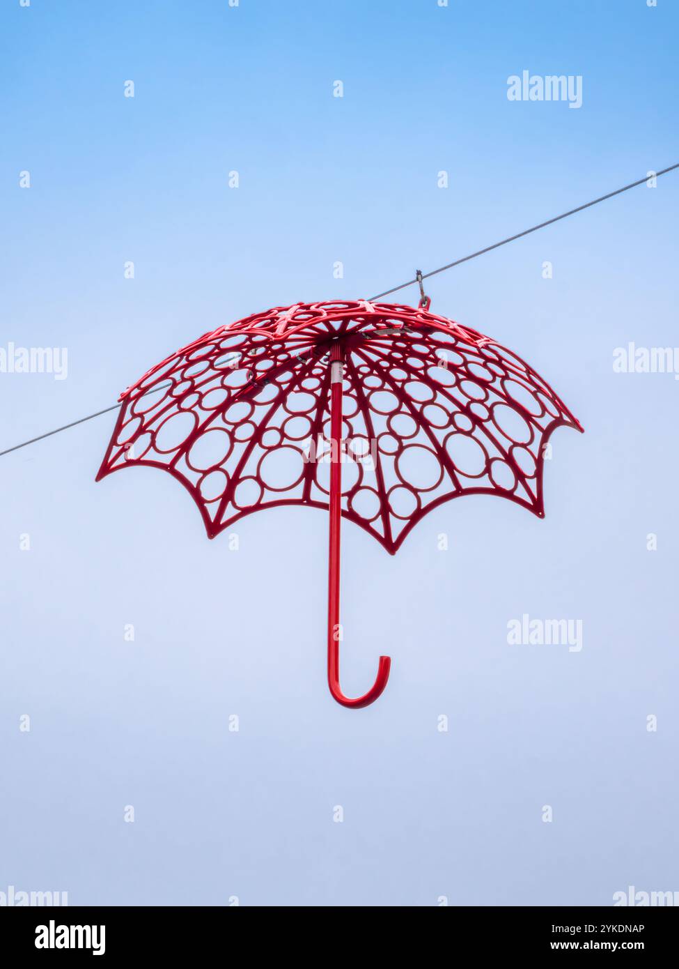 A vibrant red decorative umbrella hanging from a wire against a clear ...