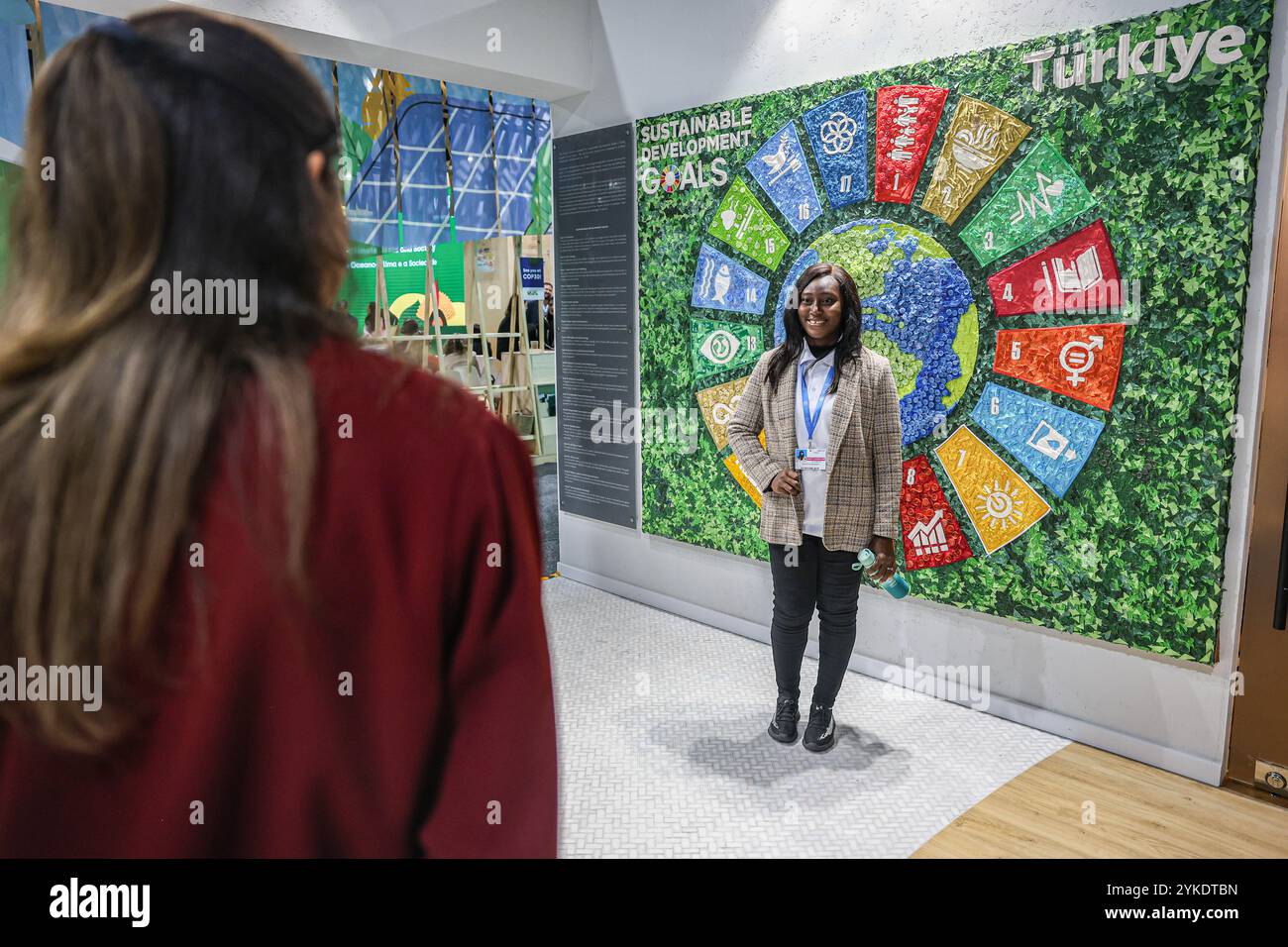 Baku, Azerbaijan, Azerbaijan. 16th Nov, 2024. A woman stands in front of an SDG billboard made ...