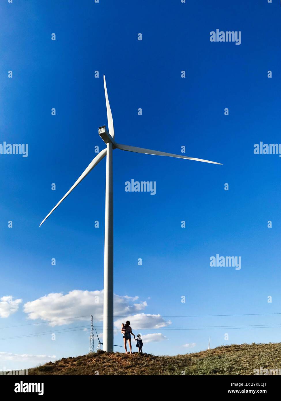 A family stands near a large wind turbine under a clear blue sky ...