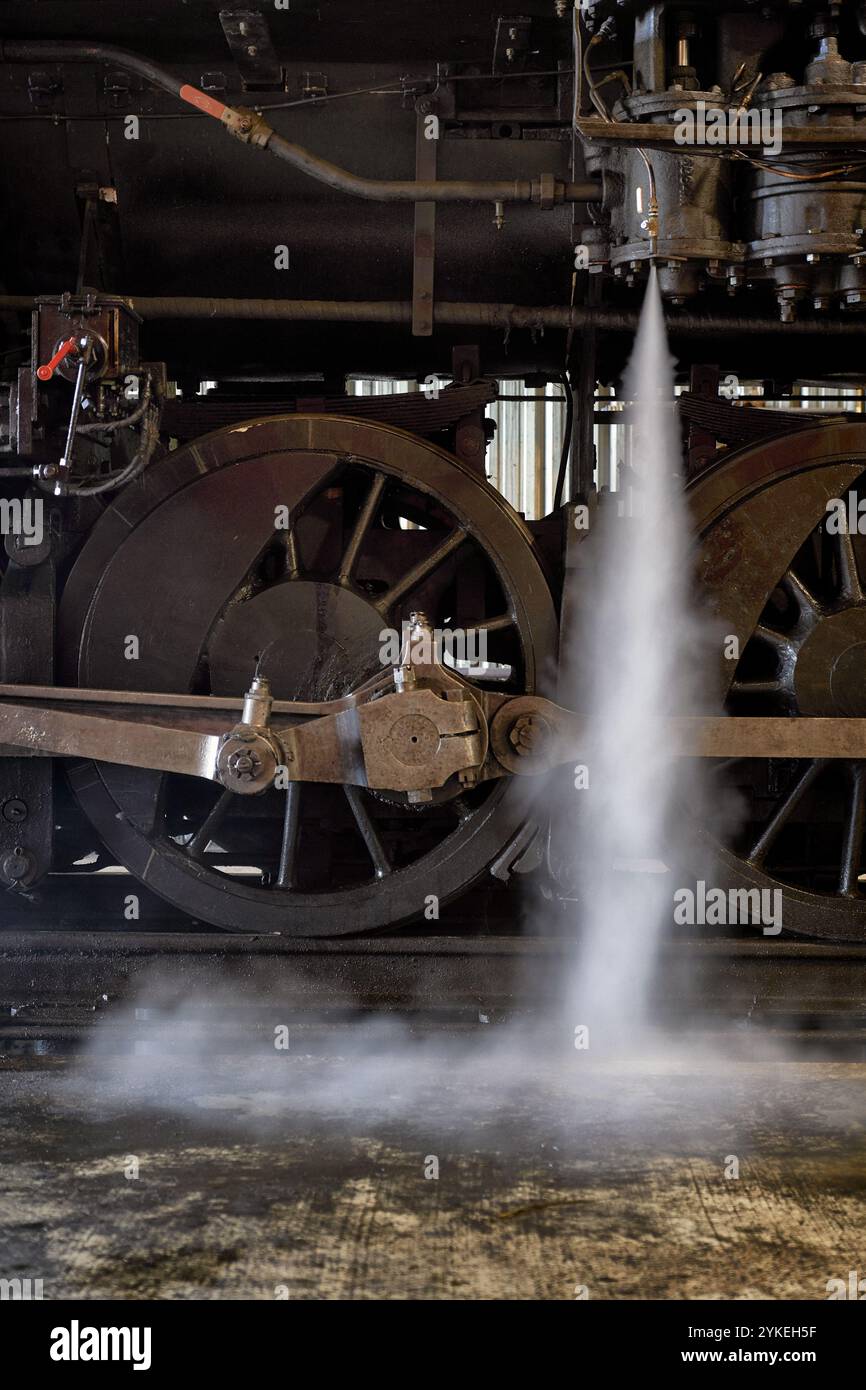 A vintage steam locomotive operates with steam escaping from its wheels ...