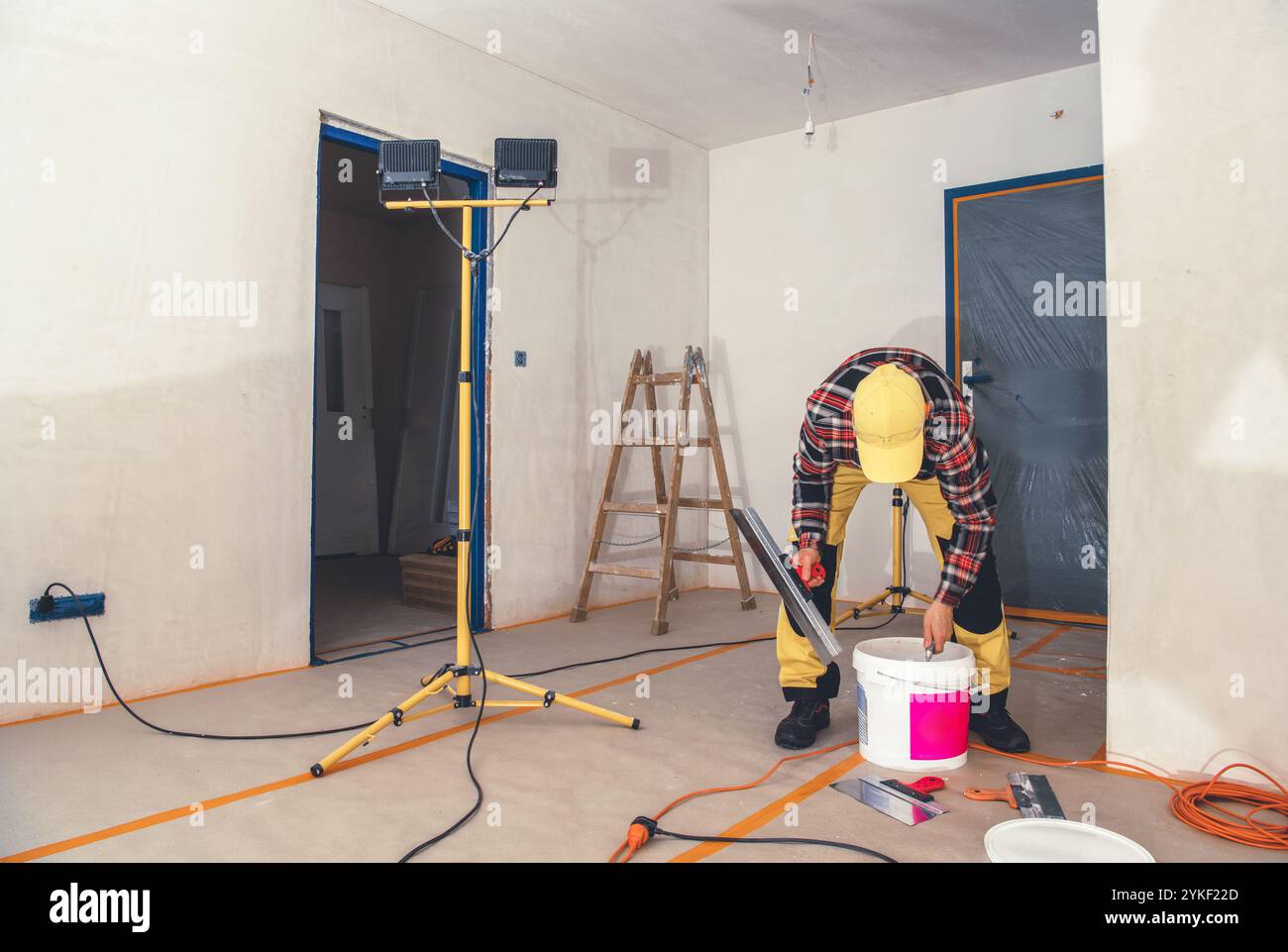 A worker is mixing paint in a bucket while preparing to paint walls in ...