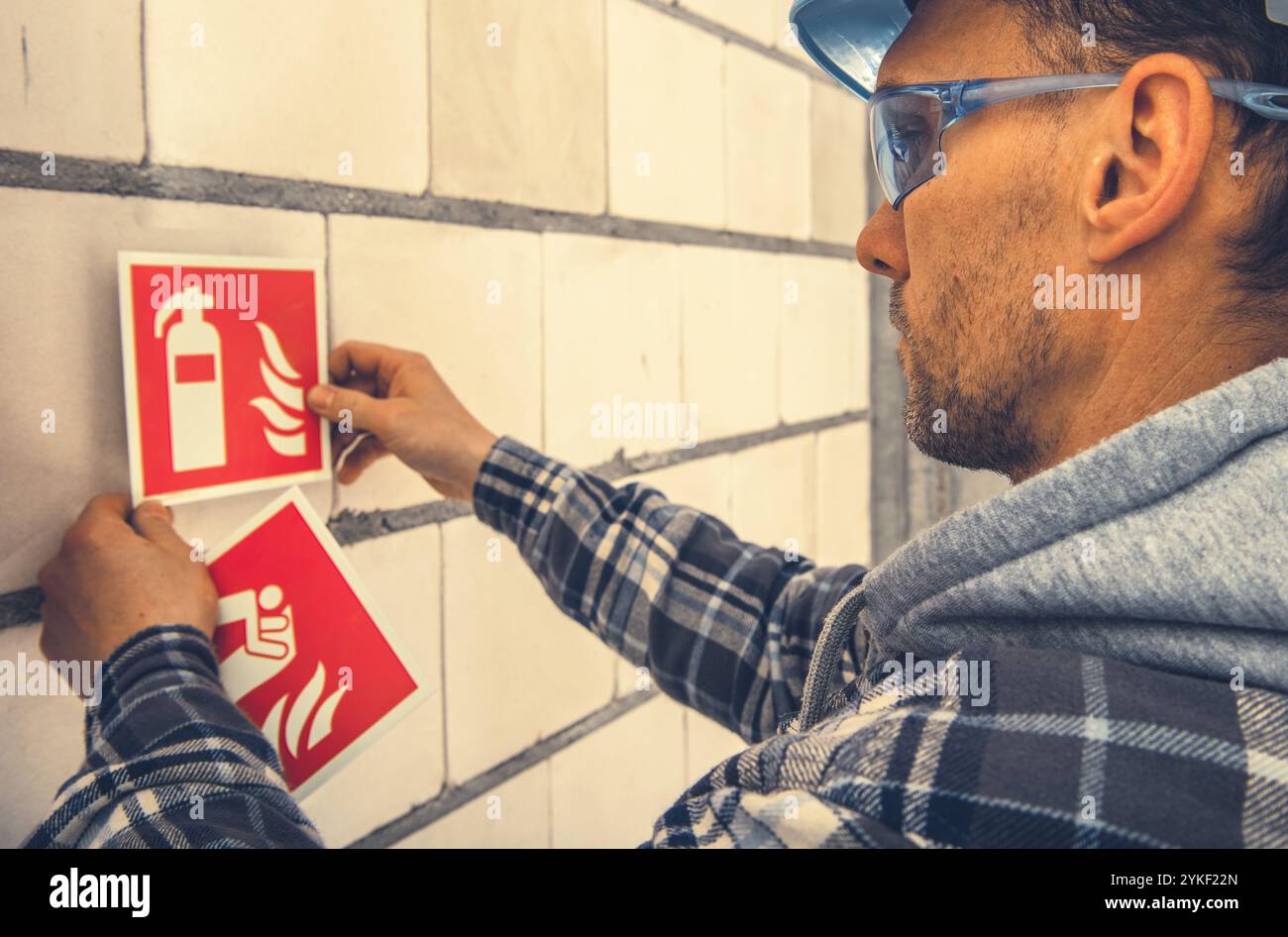 A worker attaches essential fire safety signs to a wall at a ...
