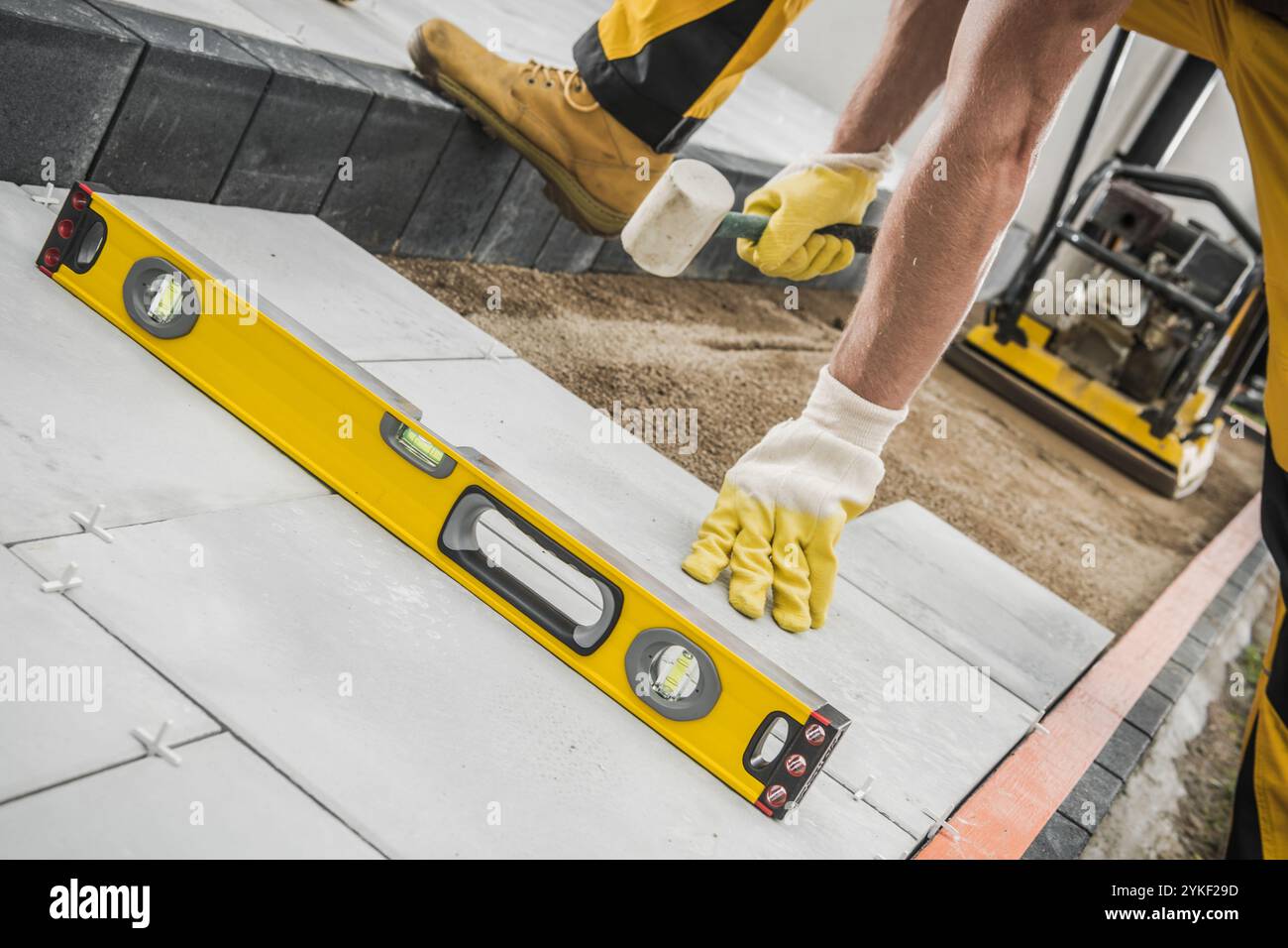 A construction worker carefully checks the alignment of pavers using a ...