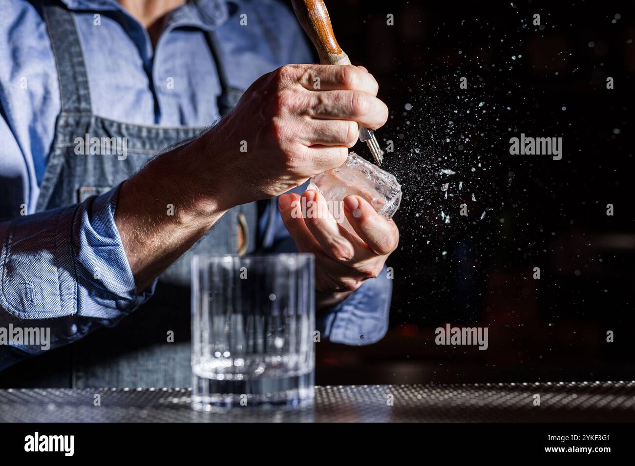 A bartender skillfully carves a block of ice to create the perfect ...