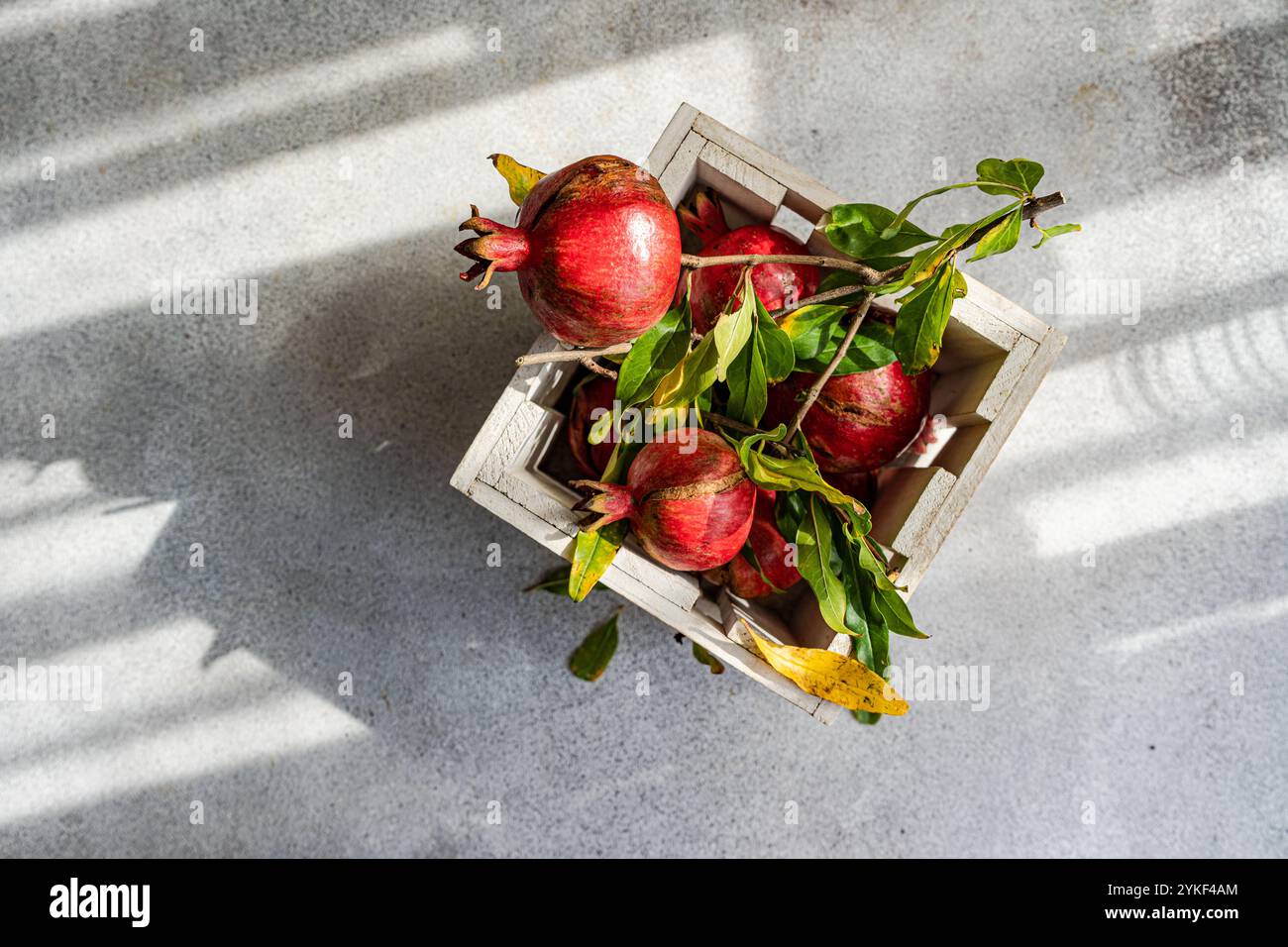Top view of a wooden crate filled with ripe red pomegranates surrounded ...