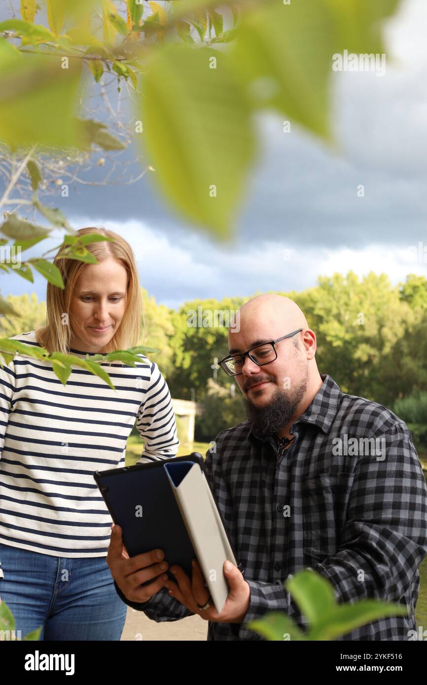 A trans man and a woman calmly engage with a tablet together outdoors ...