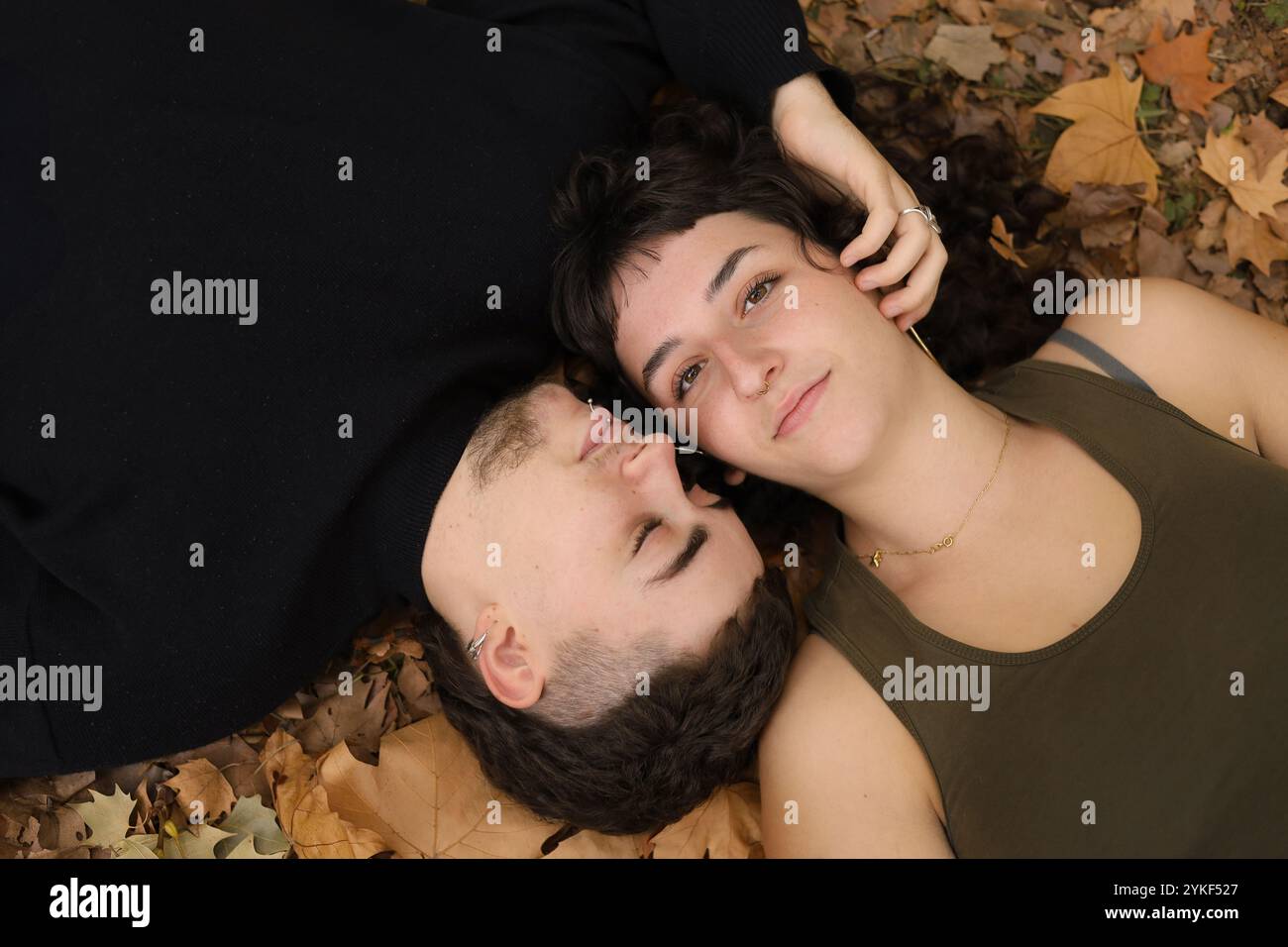 A tender scene of a LGBTQIA+ couple lying on fall leaves, showcasing an ...