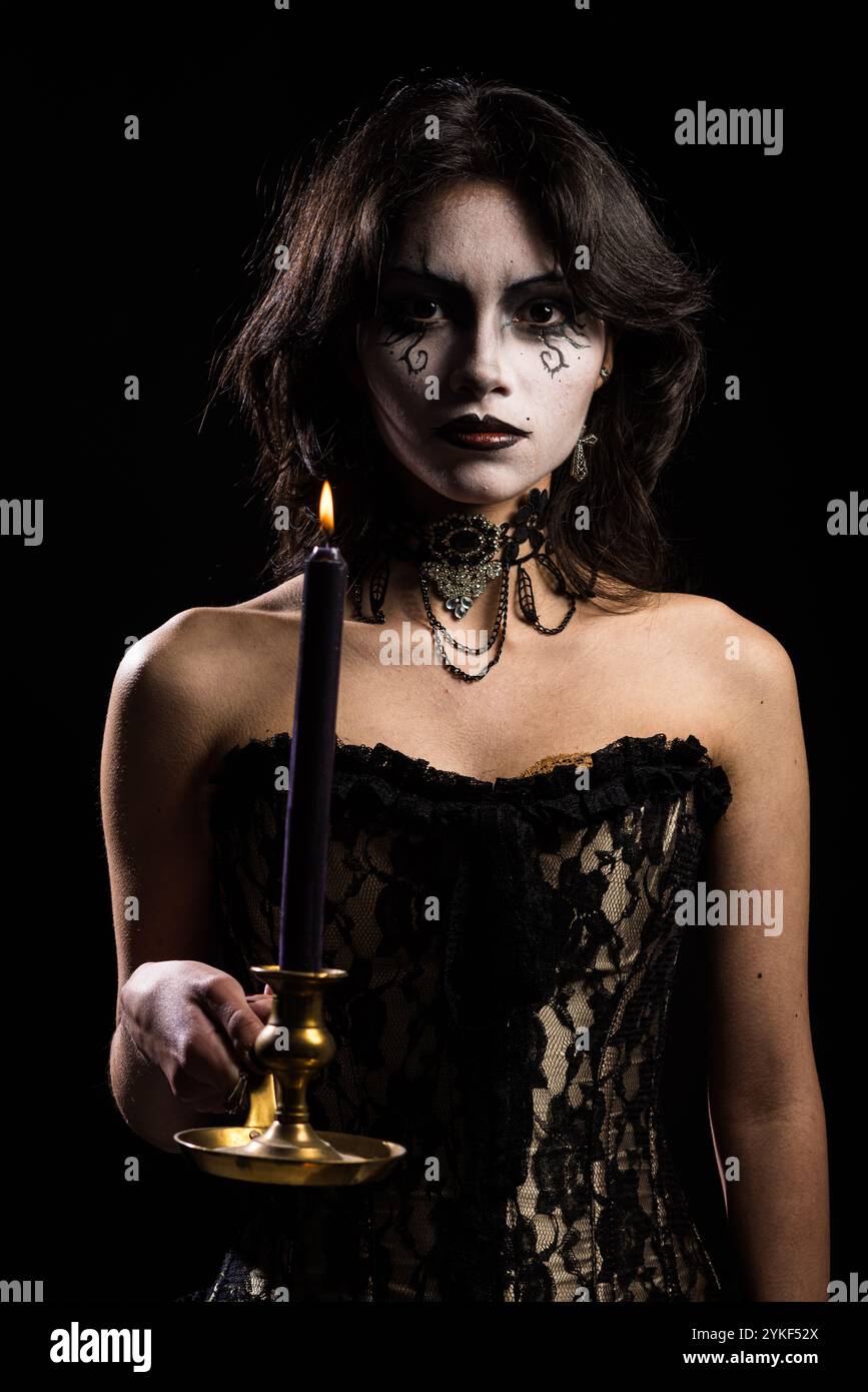 A gothic woman with dramatic makeup and a black lace dress holds a lit ...