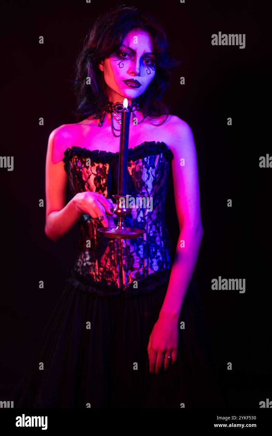 A gothic woman stands in a dimly lit setting, holding a candle She ...