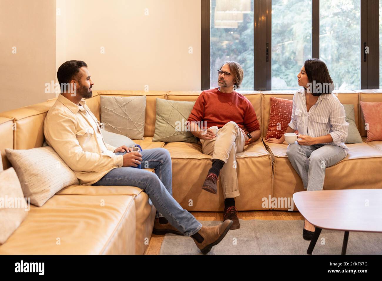 A relaxed meeting in a coworking space where three individuals casually ...