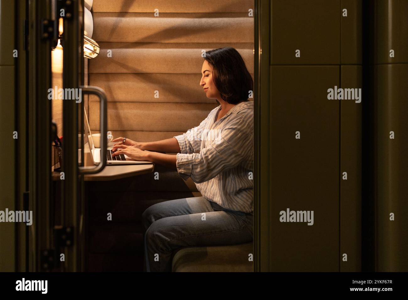 A person working intently on a laptop in a cozy, private booth within a ...