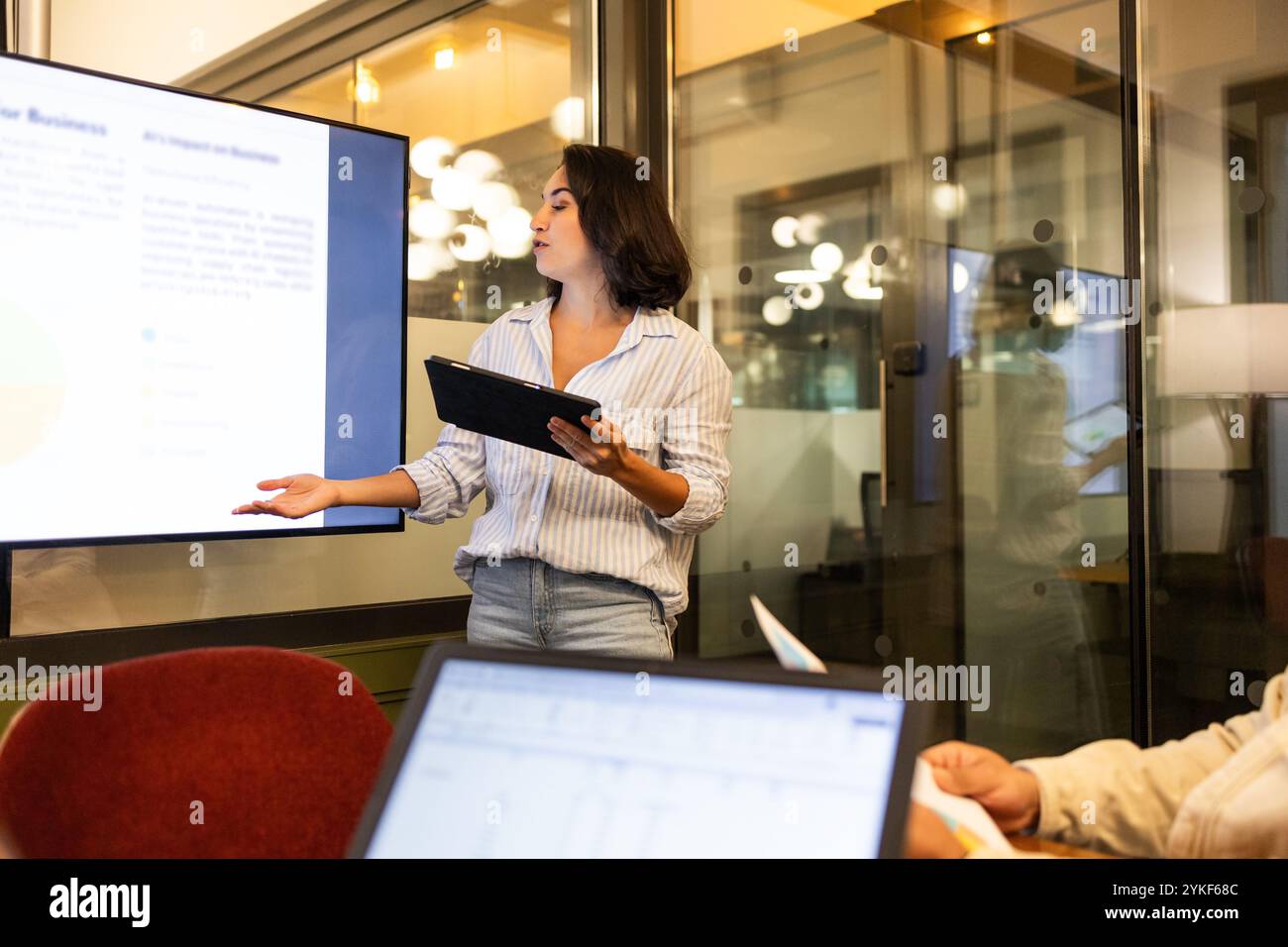A woman presents confidently with a tablet in a modern coworking space ...