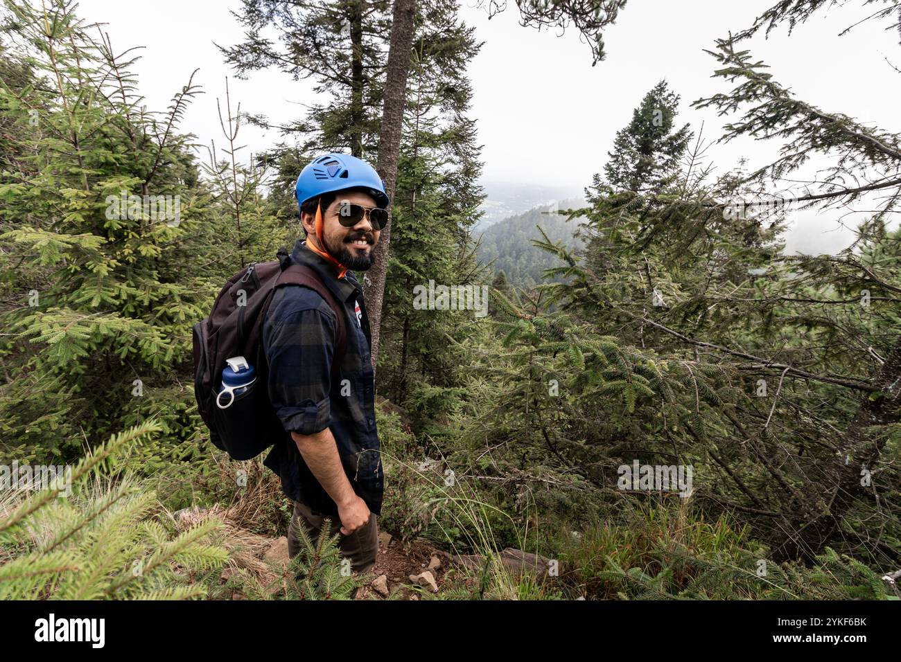 A smiling hiker wearing a blue helmet and sunglasses stands among ...
