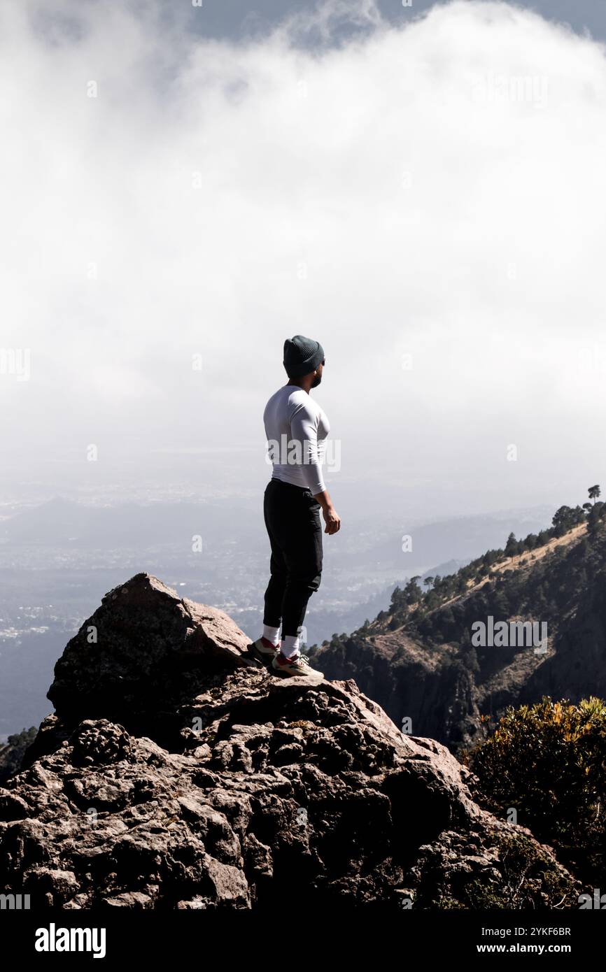 A hiker stands on a rocky peak, gazing out at a sweeping mountain view ...