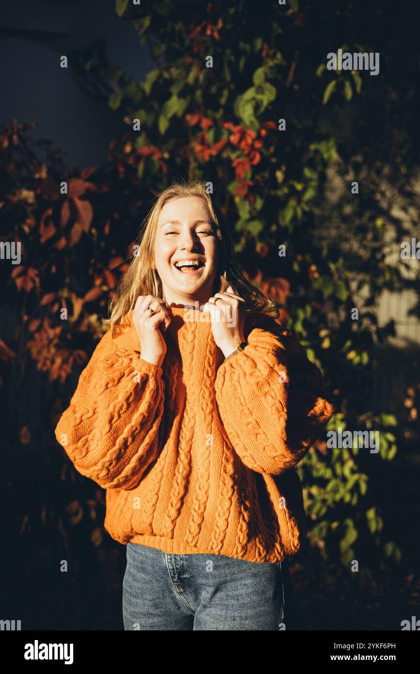 A woman joyfully poses in a cozy, knitted orange sweater amidst vibrant ...