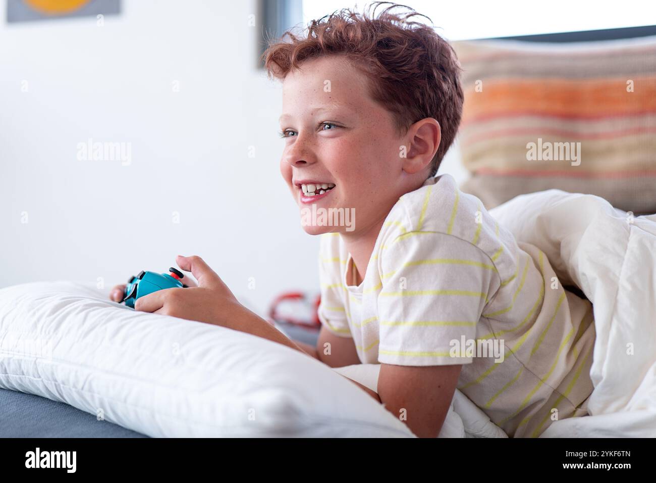 A joyful male child gamer sitting comfortably on a white couch while ...