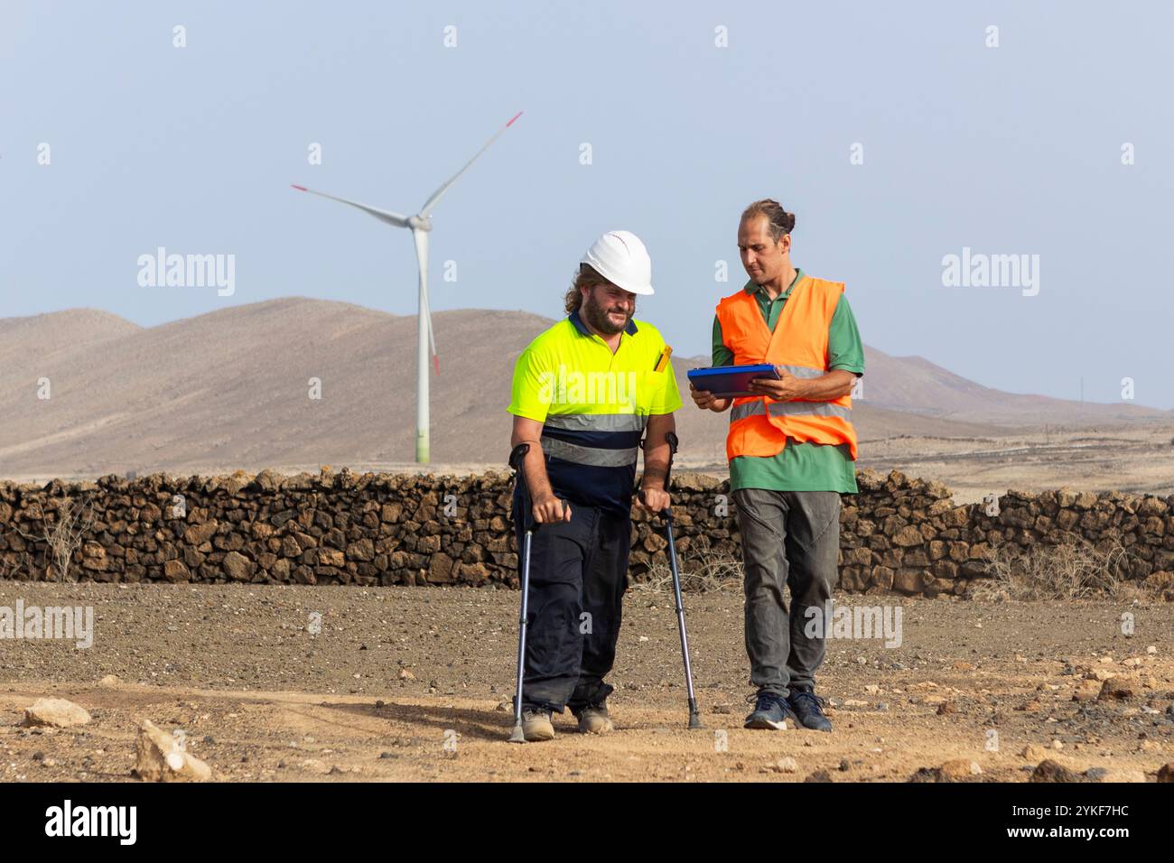 A disabled worker on crutches and another man discuss renewable energy safety protocols at a ...