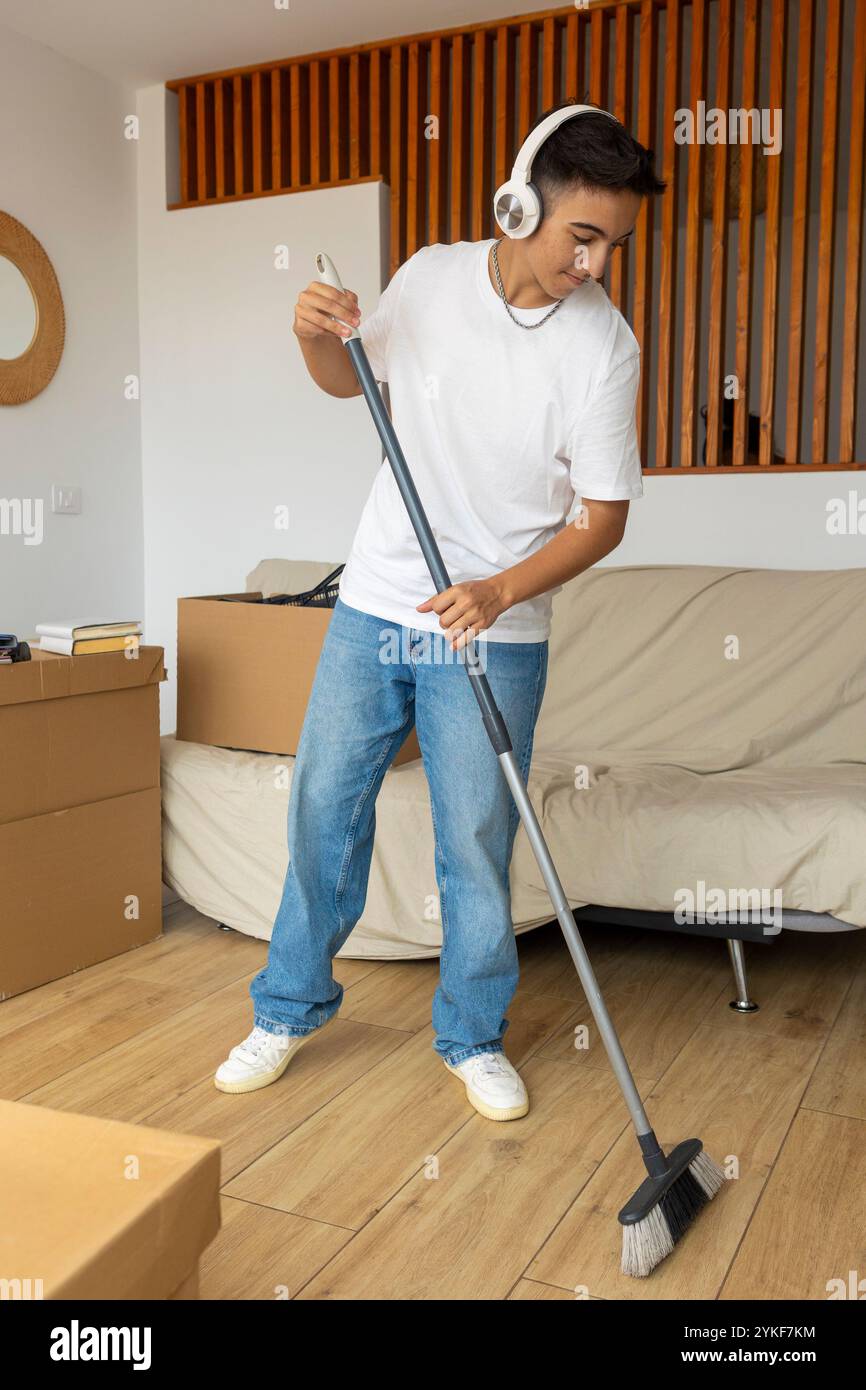 A young trans man sweeps the floor of his new home, wearing headphones ...