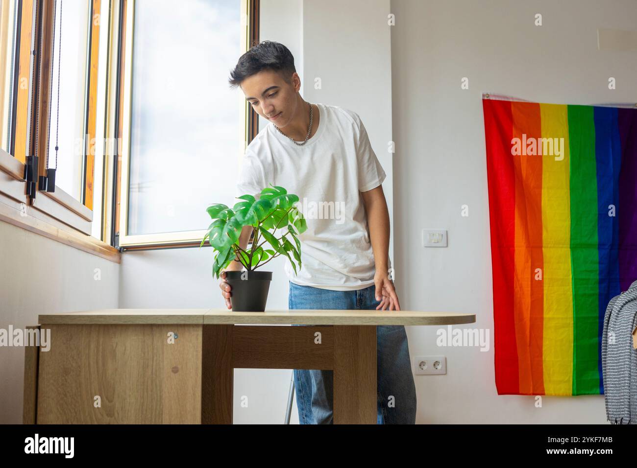 A trans man sets up his home, placing a potted plant on the table with ...