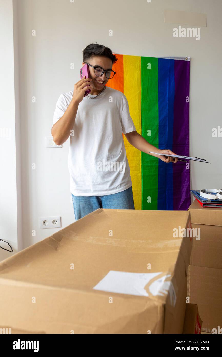 A trans man talks on the phone while holding a clipboard, smiling in a ...