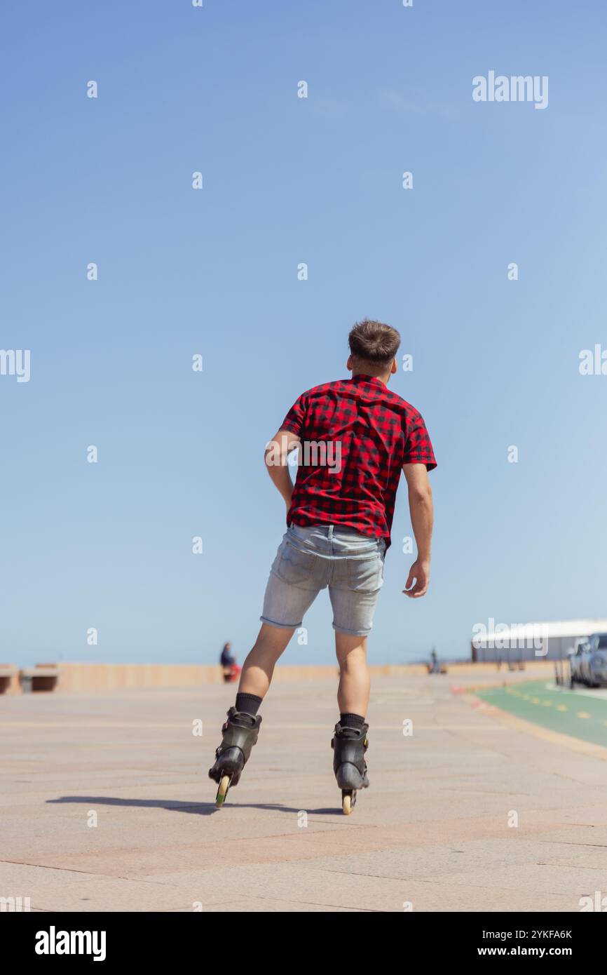 Back view of an unrecognizable young man rollerblading on a sunny day ...