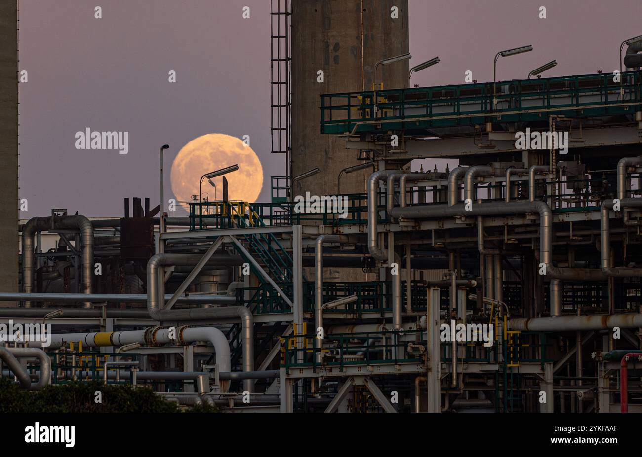 A full moon ascends behind the intricate metalwork of an industrial ...
