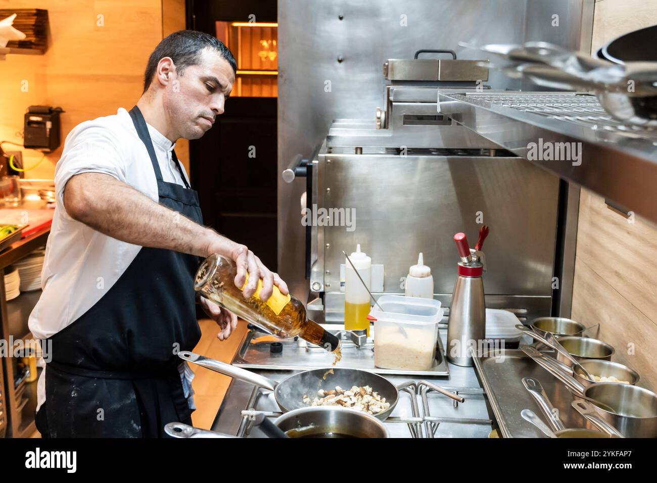 Intently focused chef pouring ingredients into a pan amid the bustling ...