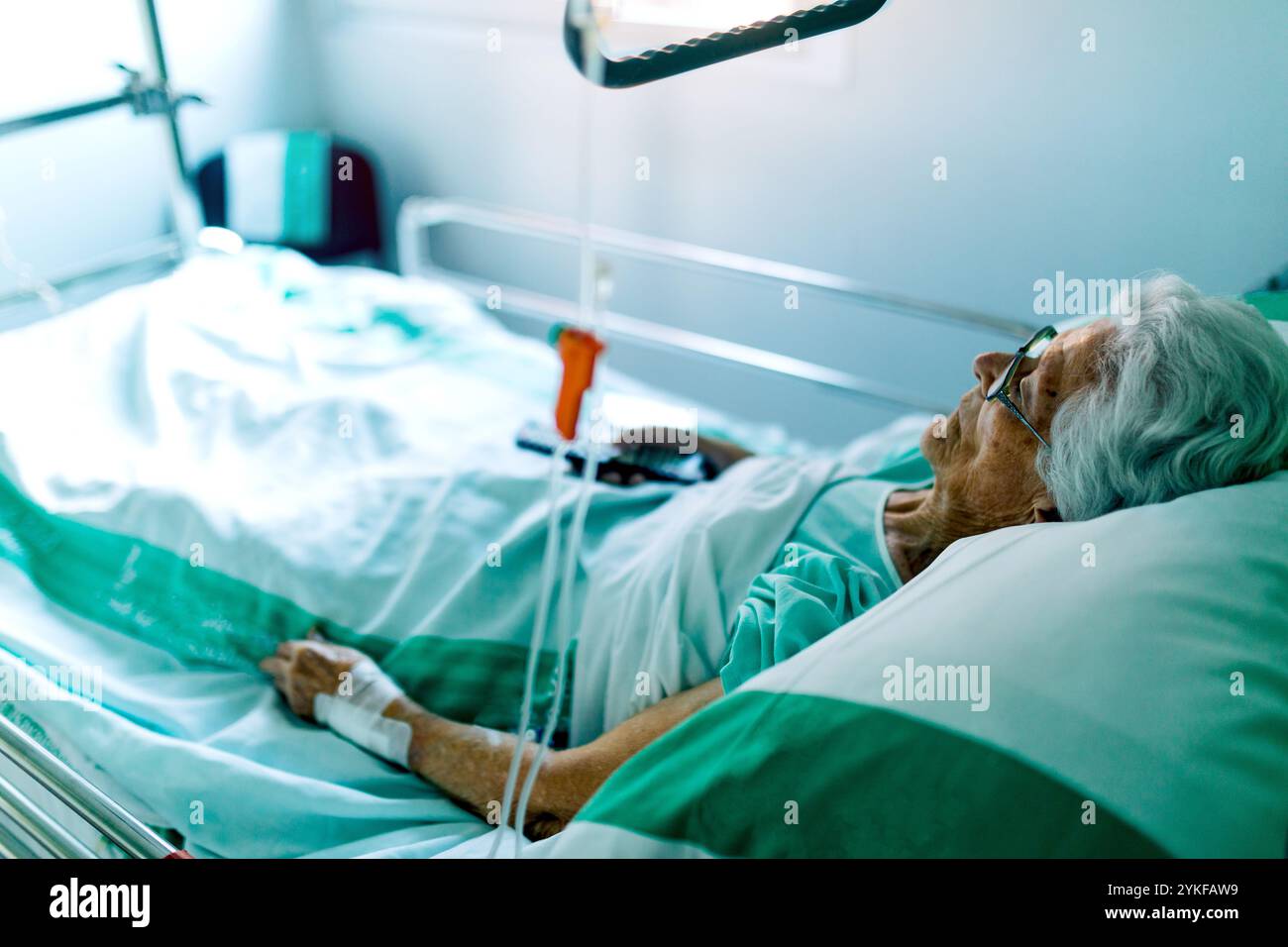 An elderly woman rests peacefully in a hospital bed, connected to an IV ...