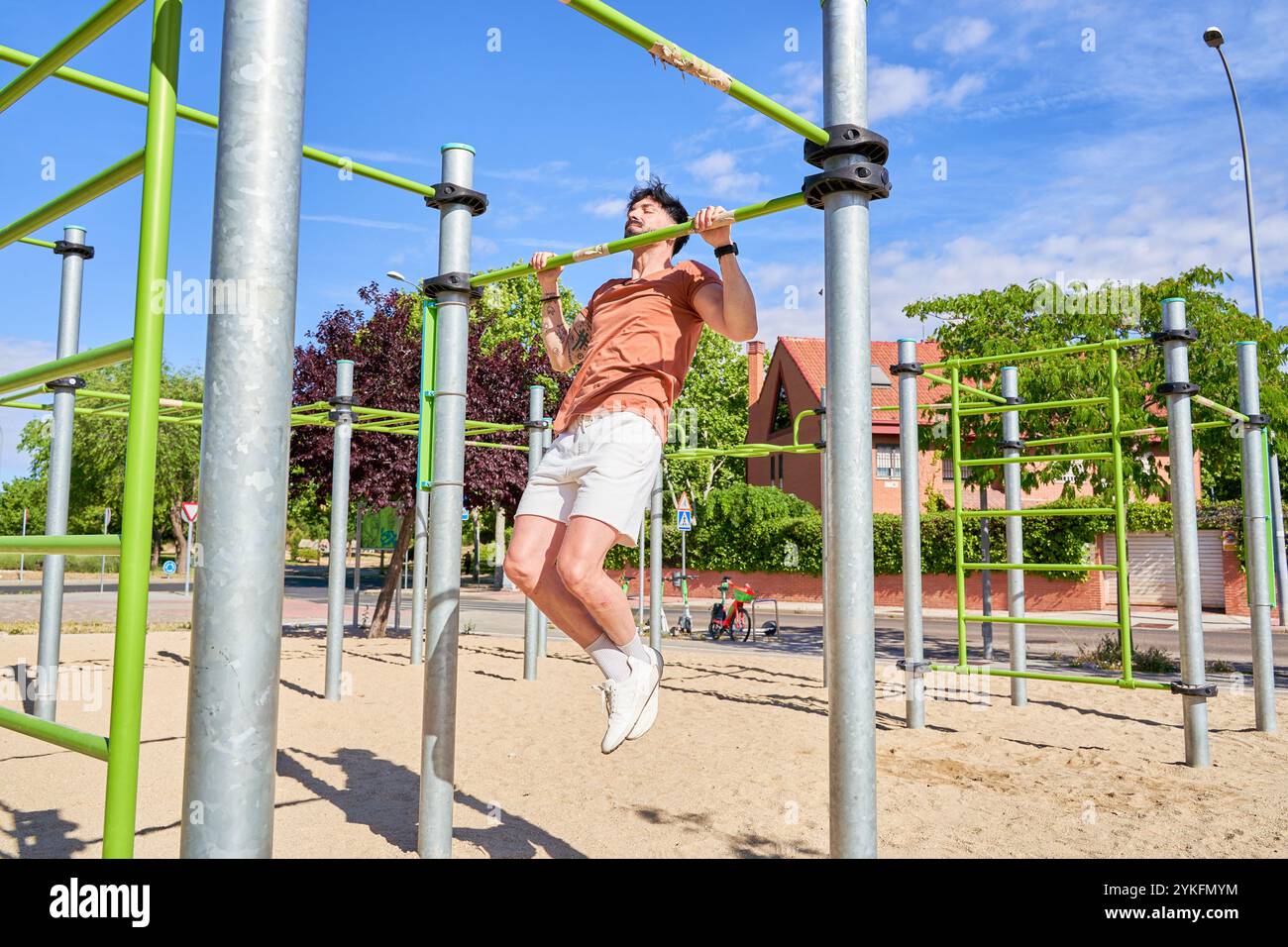 A young athlete performs pull-ups at an outdoor calisthenics park ...