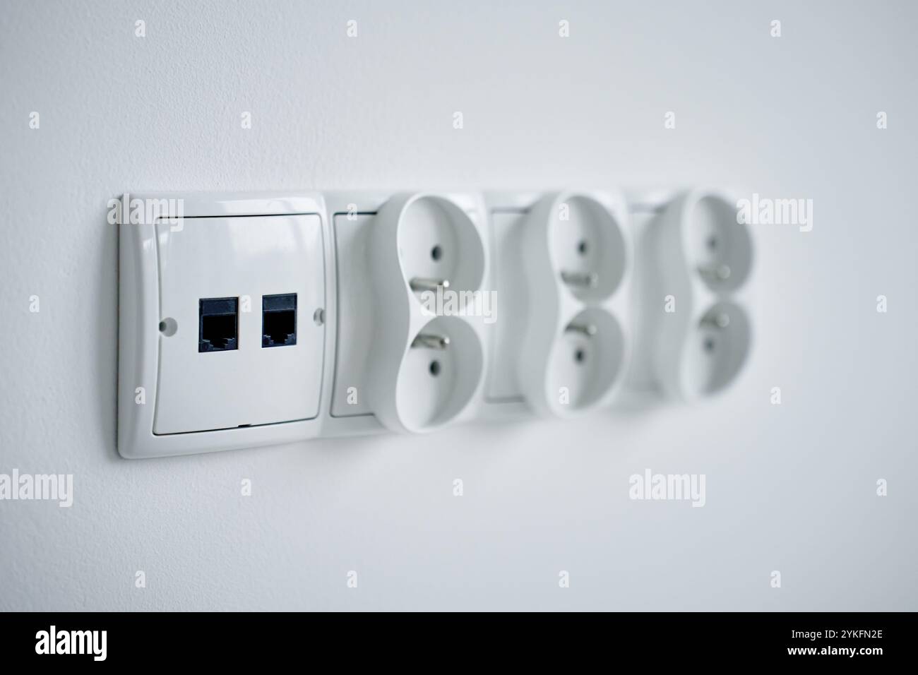 Close-up of white electrical sockets and ethernet ports on white wall ...