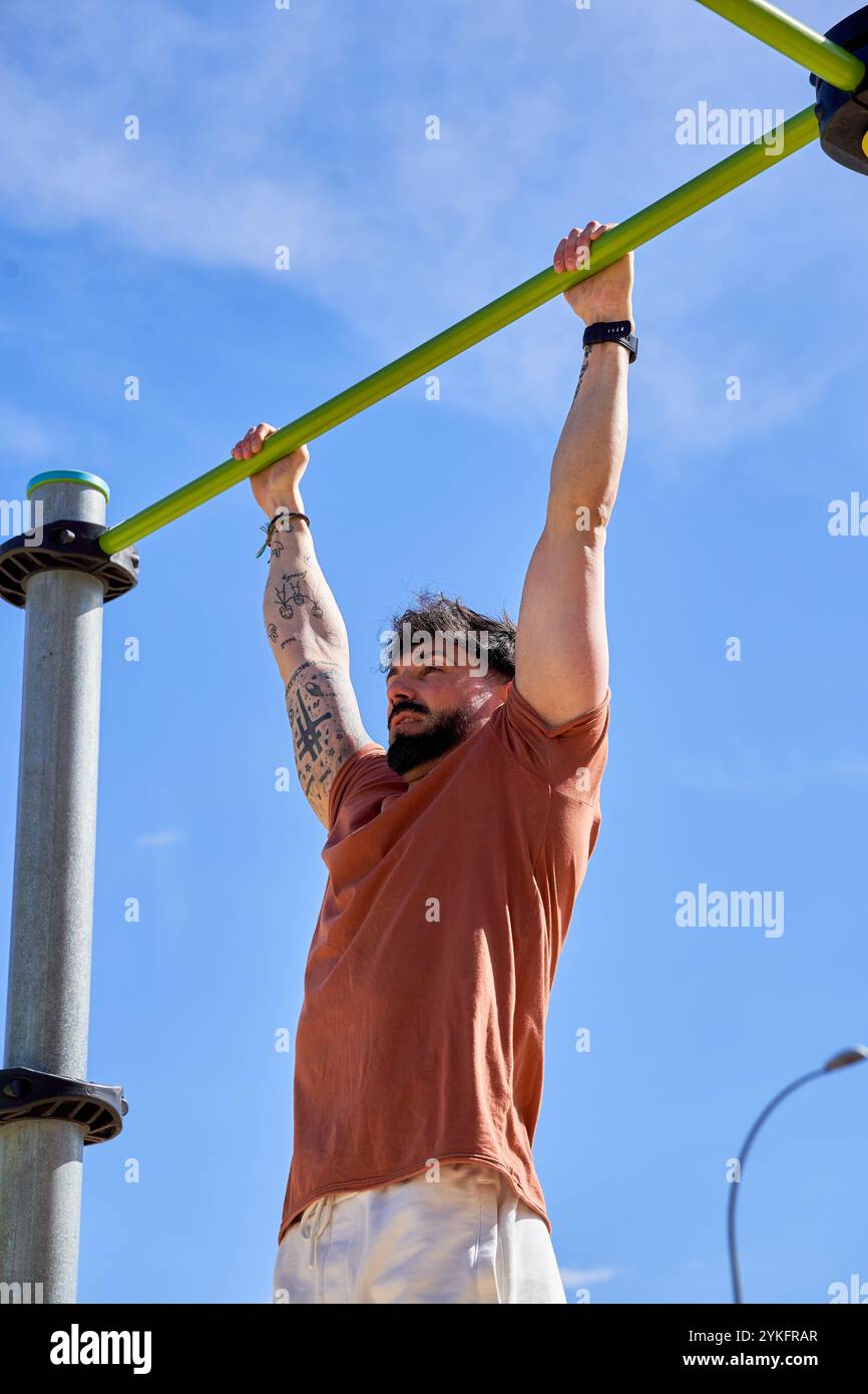 A young athlete performs pull-ups at an outdoor calisthenics park ...