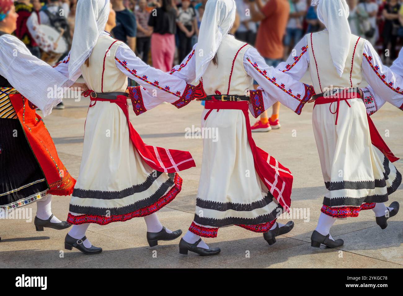 Women in white traditional dresses with red accents during folk dance ...